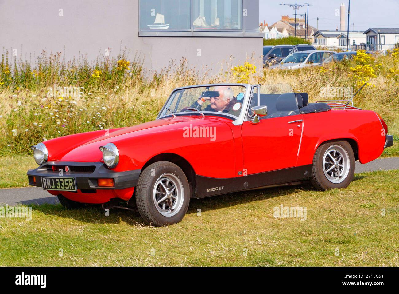 A vintage red MG midget convertible car is parked on a grassy area ...