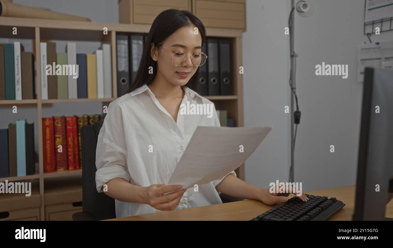 Young chinese woman working indoors in an office setting, reading a ...