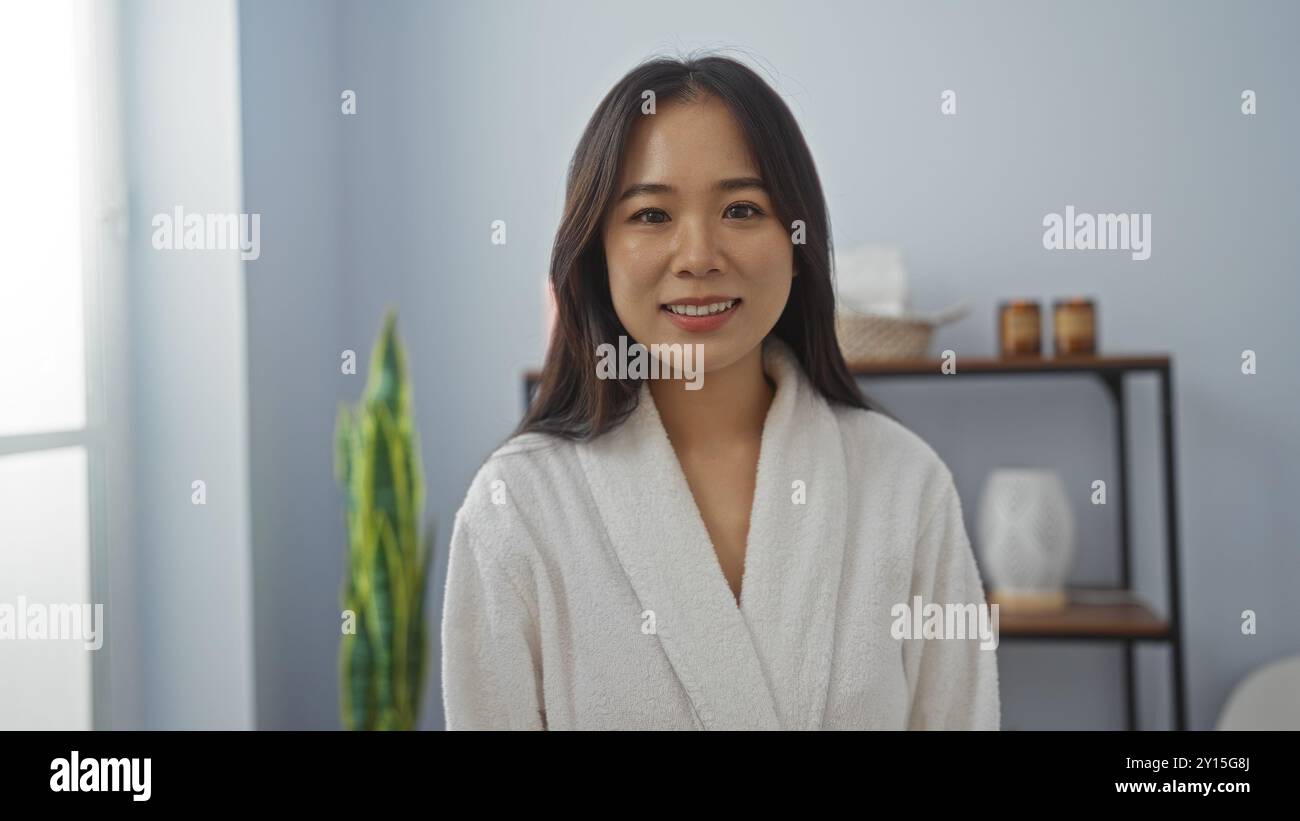 Young chinese woman in a spa wearing a white robe, smiling and standing ...