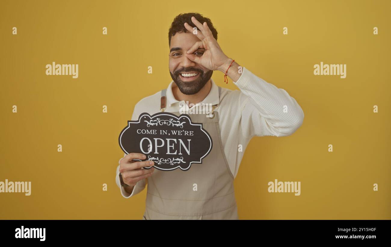 A cheerful bearded man holds an 'open' sign over a yellow background ...