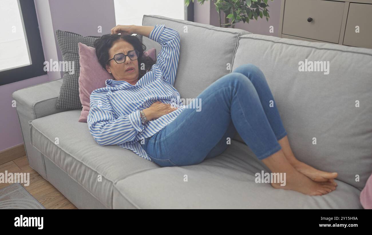 A middle-aged woman relaxes barefoot on a sofa in a well-decorated ...