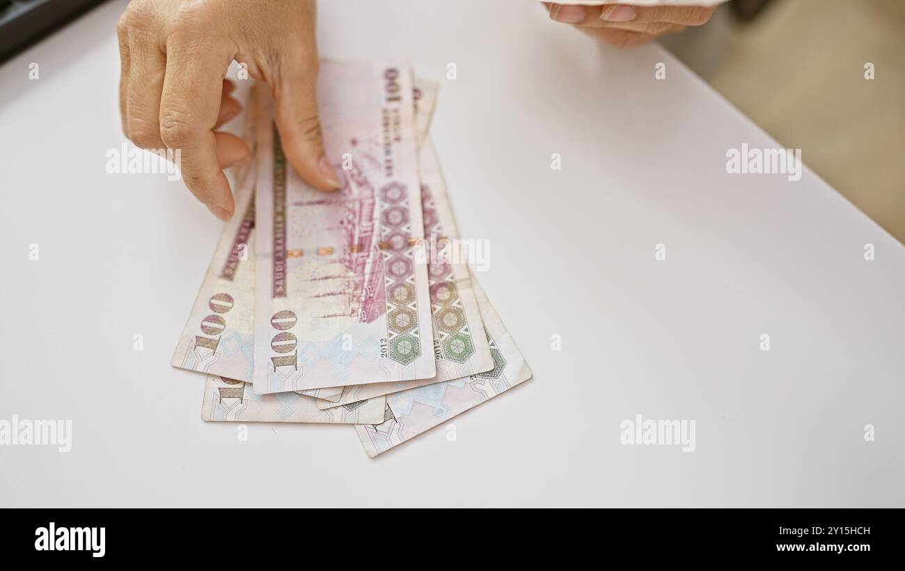 Adult woman's hands counting saudi riyal banknotes on a white office ...