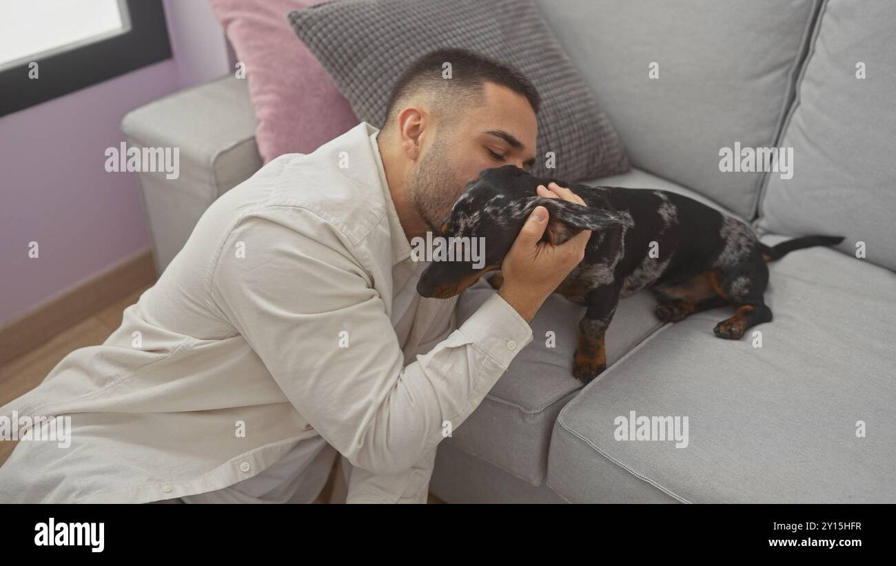 A young hispanic man gives a loving kiss to his teckel dog in a cozy ...