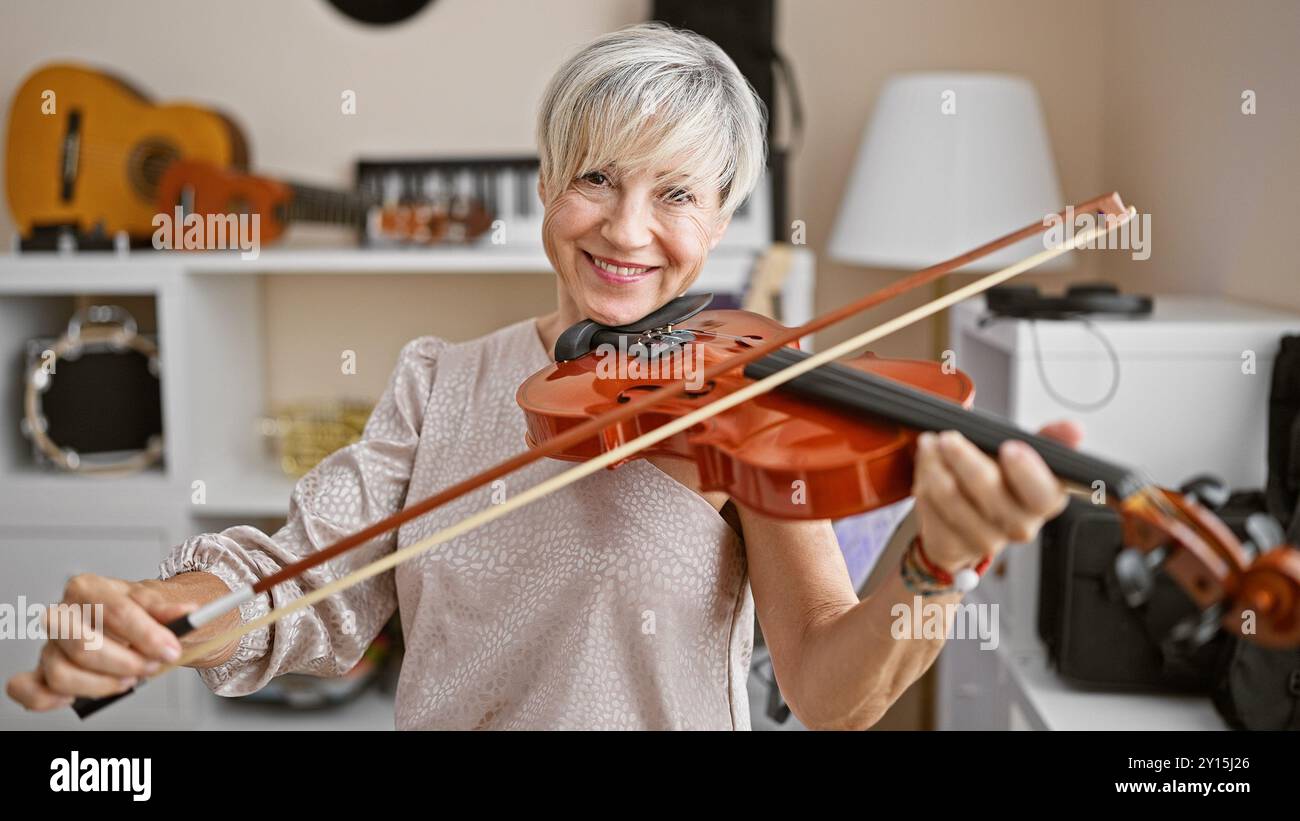 Smiling mature woman with grey hair playing violin indoors with musical ...