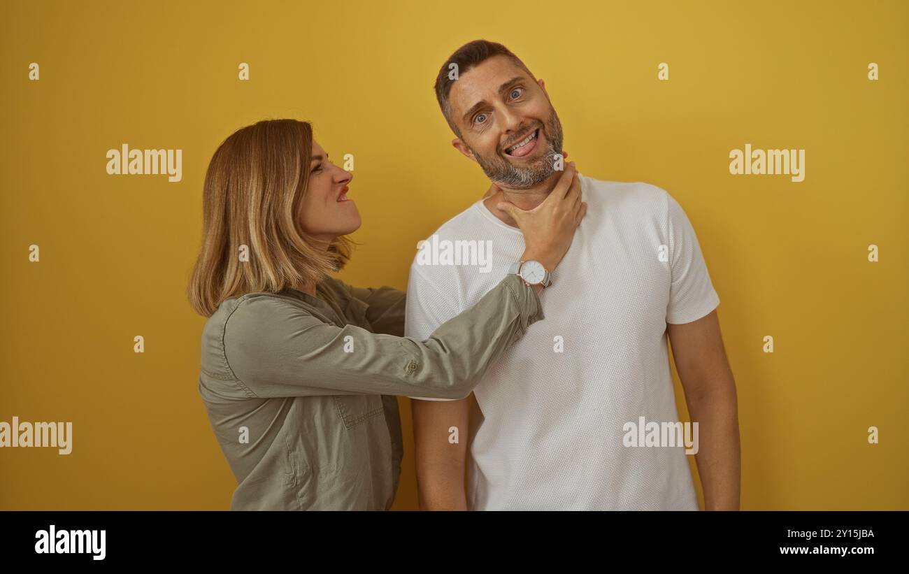 Woman playfully choking man as couple poses together against a yellow ...
