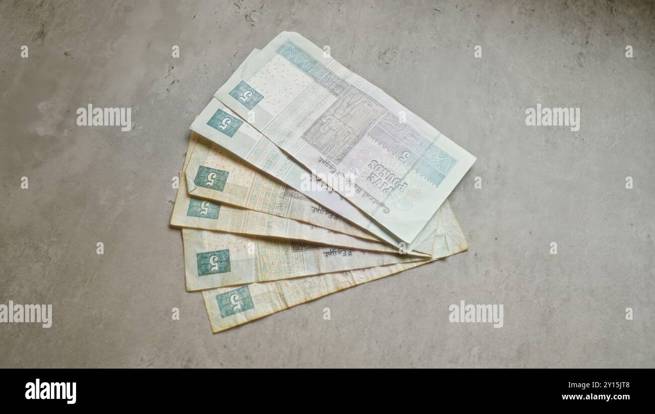 Egyptian banknotes of five pounds are spread on a concrete surface ...