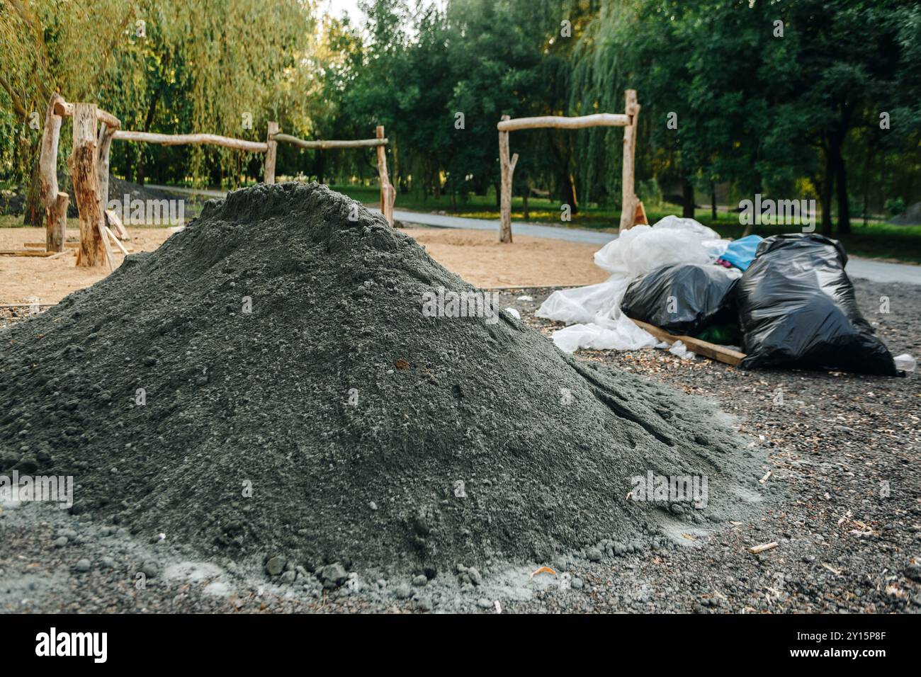 A large pile of dirt with garbage bags and wooden structures in a park ...