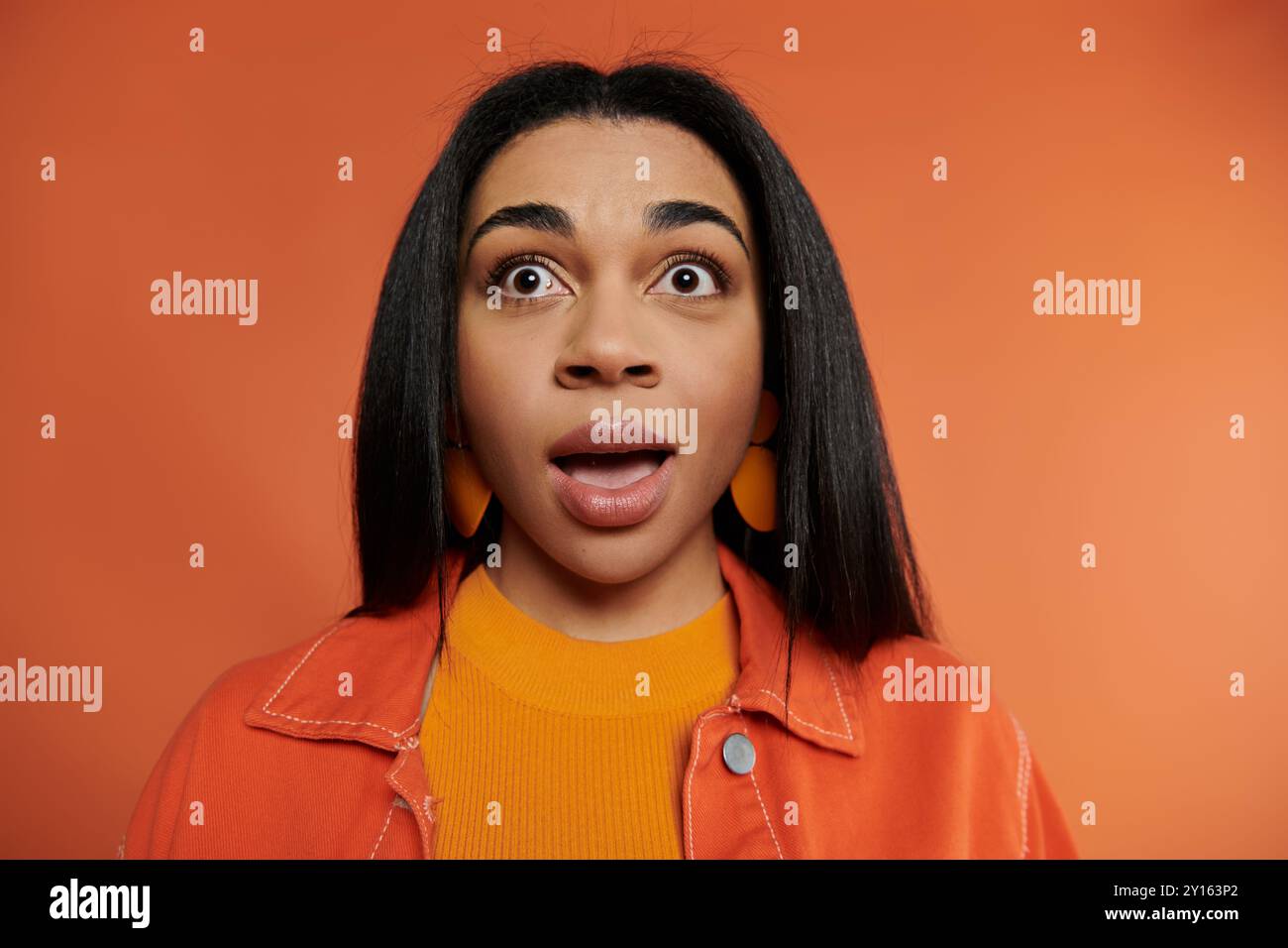 A young woman shows a look of surprise in a vibrant orange setting ...