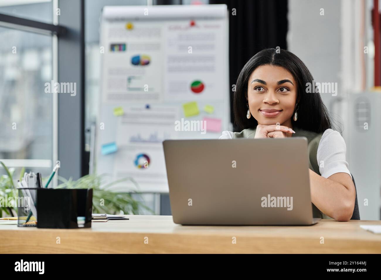 A thoughtful woman reflects while working at her desk in a vibrant ...