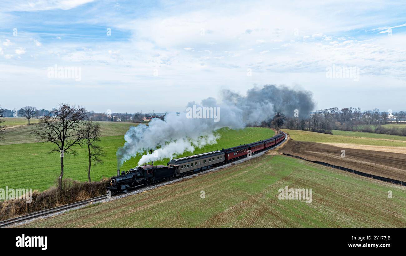 A steam train billows smoke as it travels through vibrant green fields ...