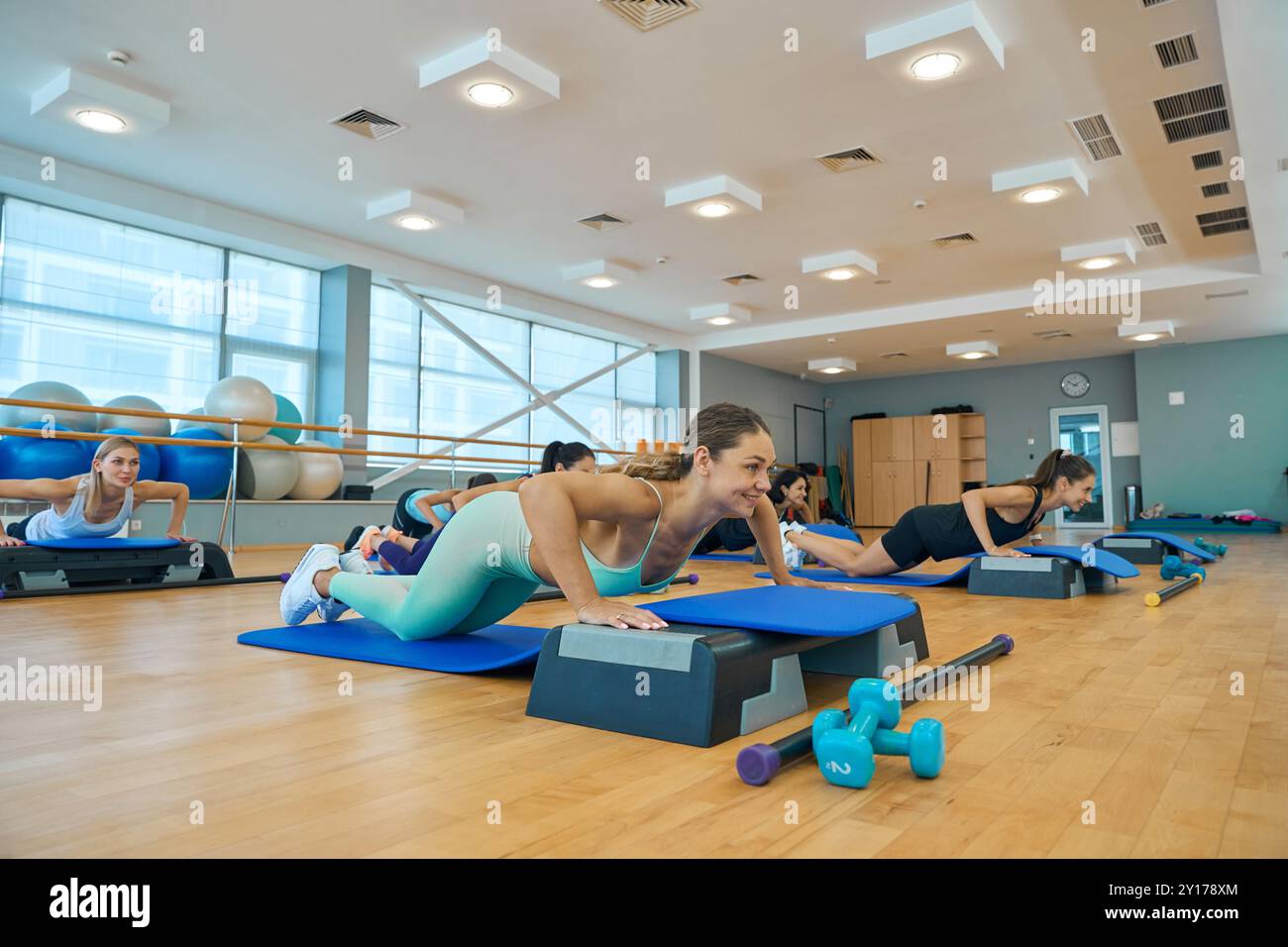 Women in training clothes perform strength exercises in spacious hall ...