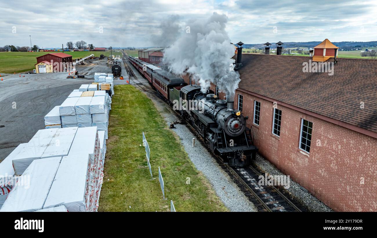 A vintage steam locomotive emits steam while departing from a brick ...