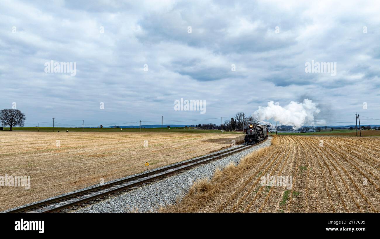 A historic steam train chugs along the tracks, billowing white smoke as ...