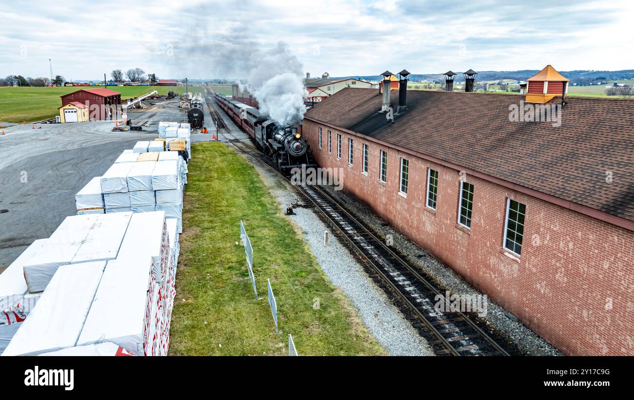 A vintage steam train puffs white smoke as it moves along the tracks ...