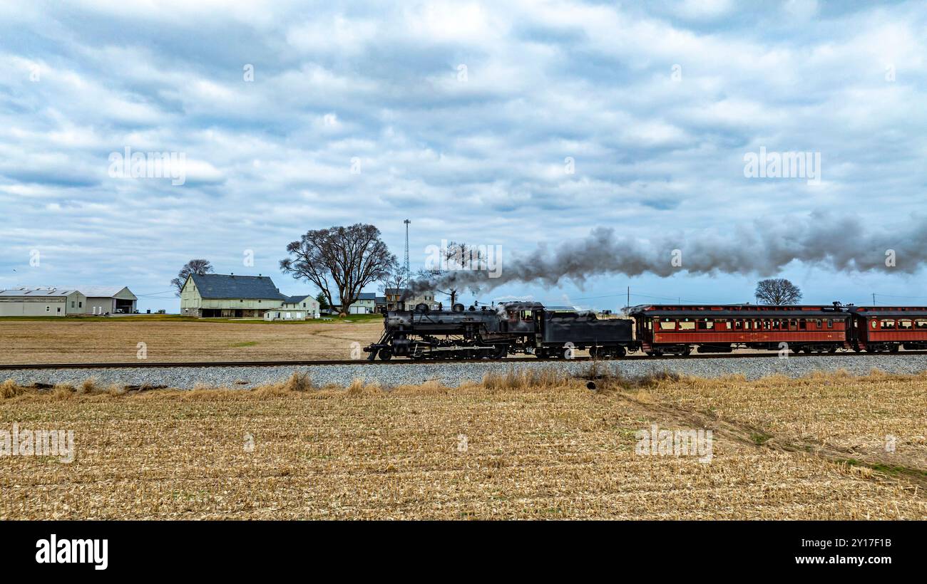 A classic steam locomotive chugs along the tracks, trailing puffs of ...