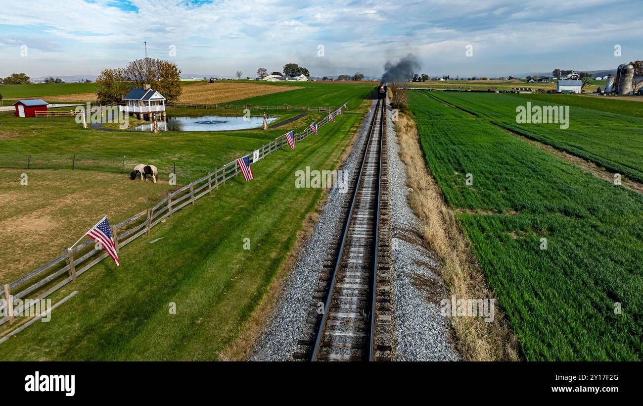 A steam train moves along railway tracks surrounded by green fields and ...