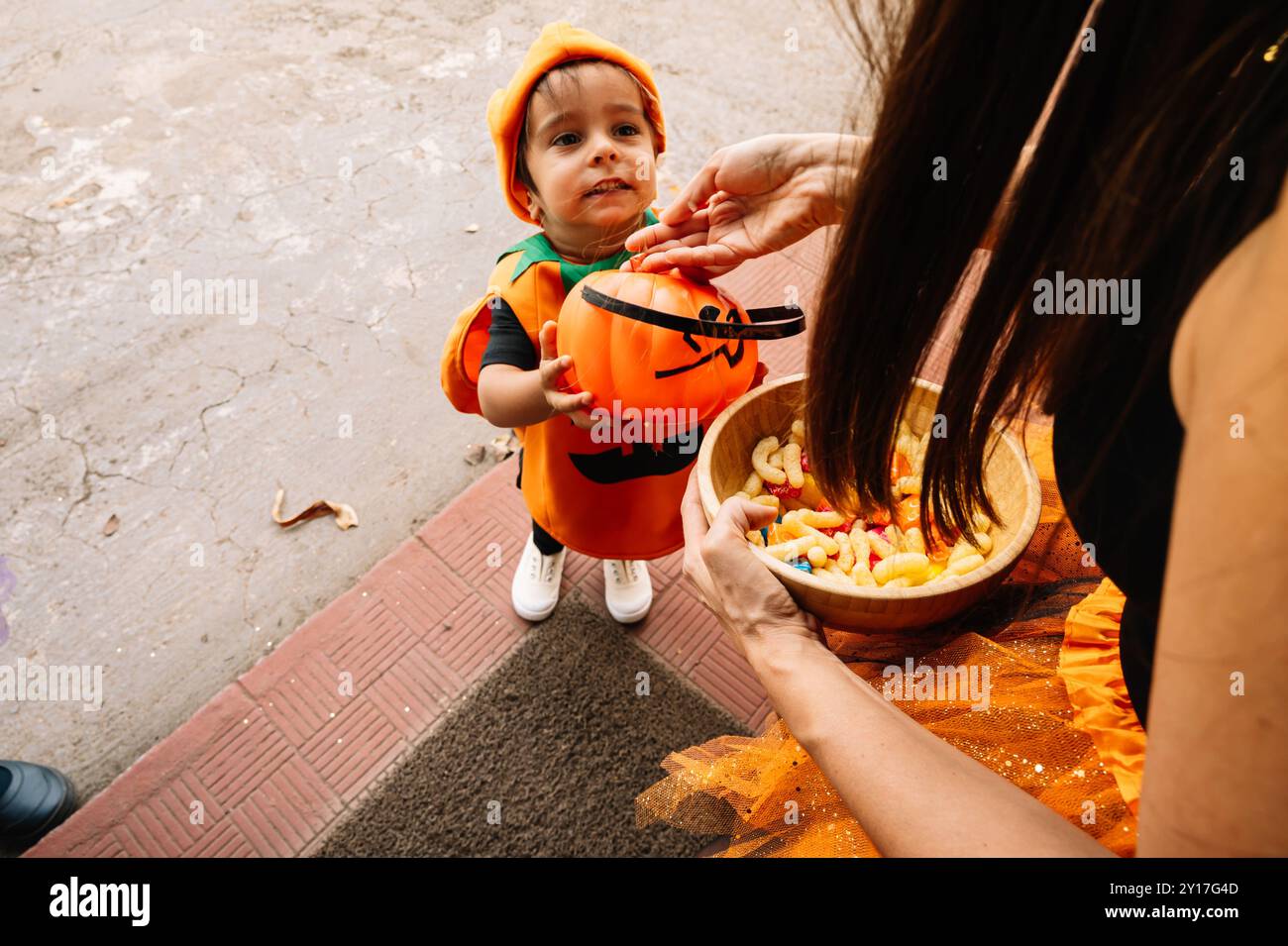 A woman holds a bowl of candy for a child in a Halloween costume as he ...