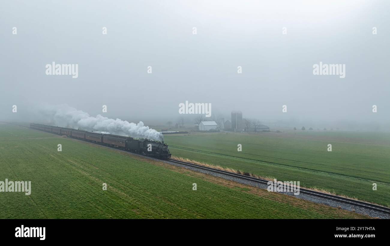 A steam locomotive moves along the tracks, shrouded by thick fog, with ...