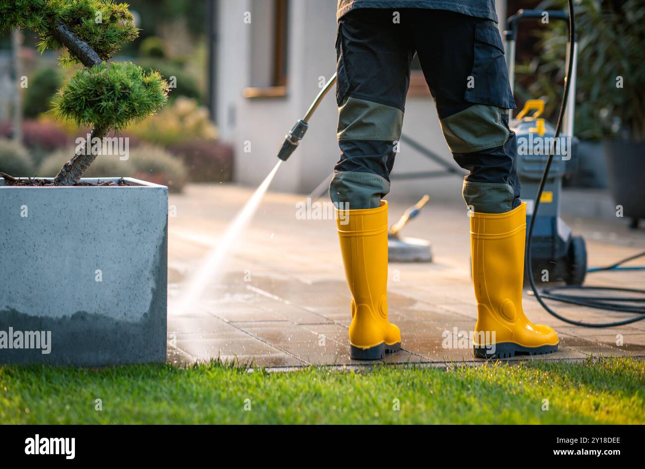 A person wearing yellow rubber boots operates a pressure washer ...