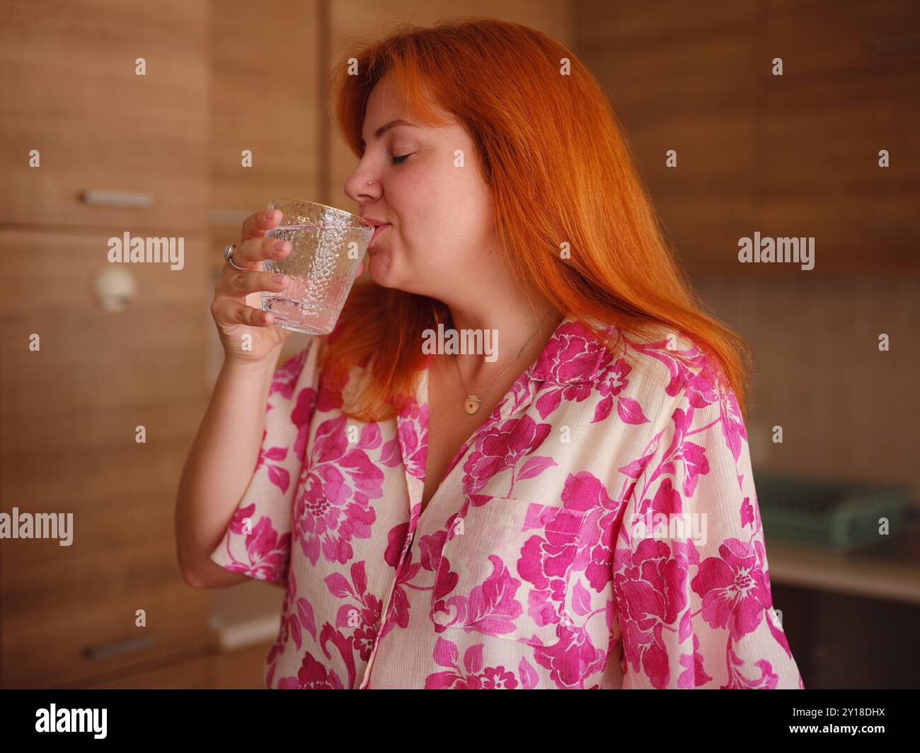 Thirsty young woman drinking fresh water from glass. Home office kitchen interior. Dehydration ...