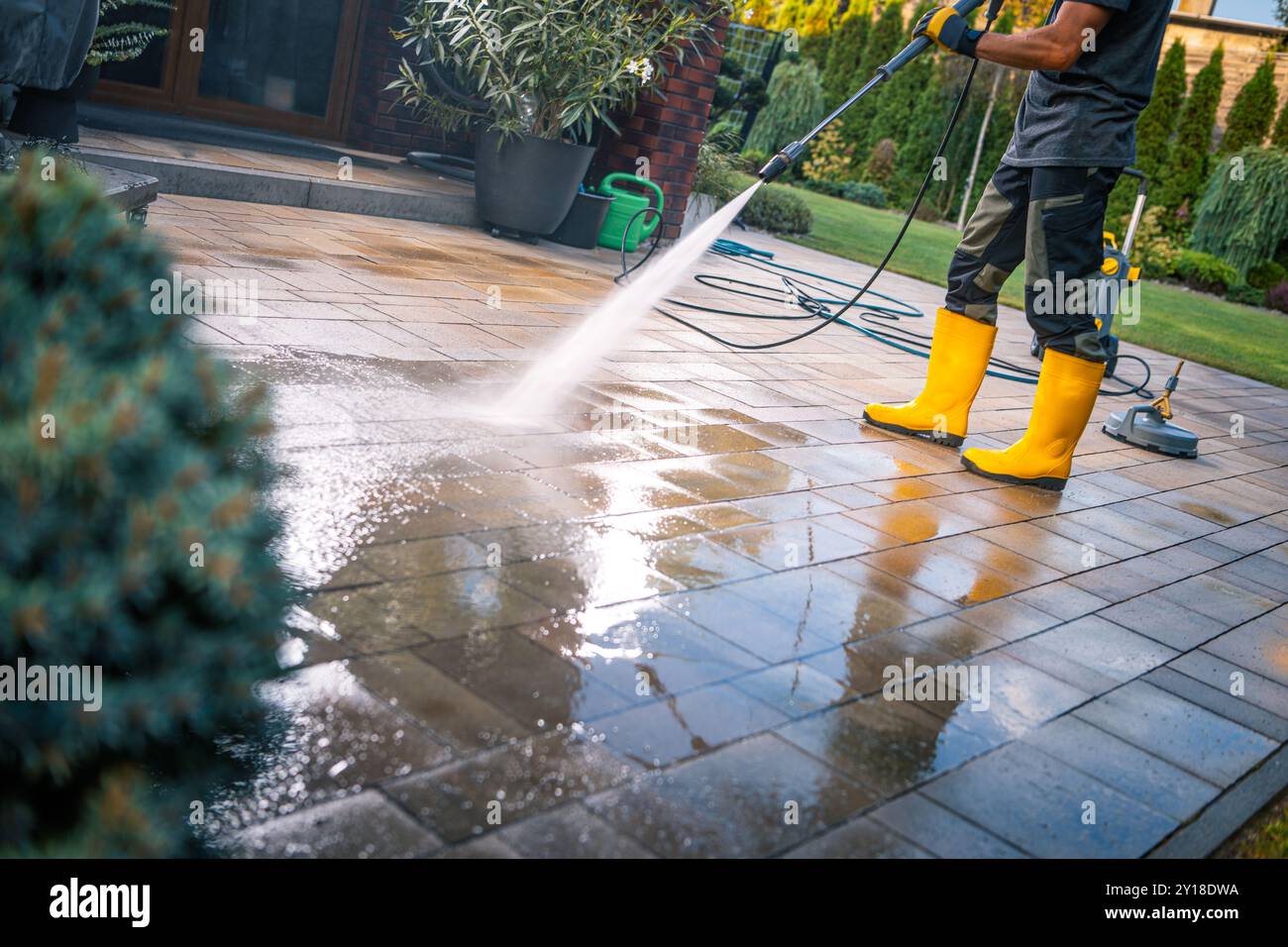 A worker uses a pressure washer to clean the patio, surrounded by a ...
