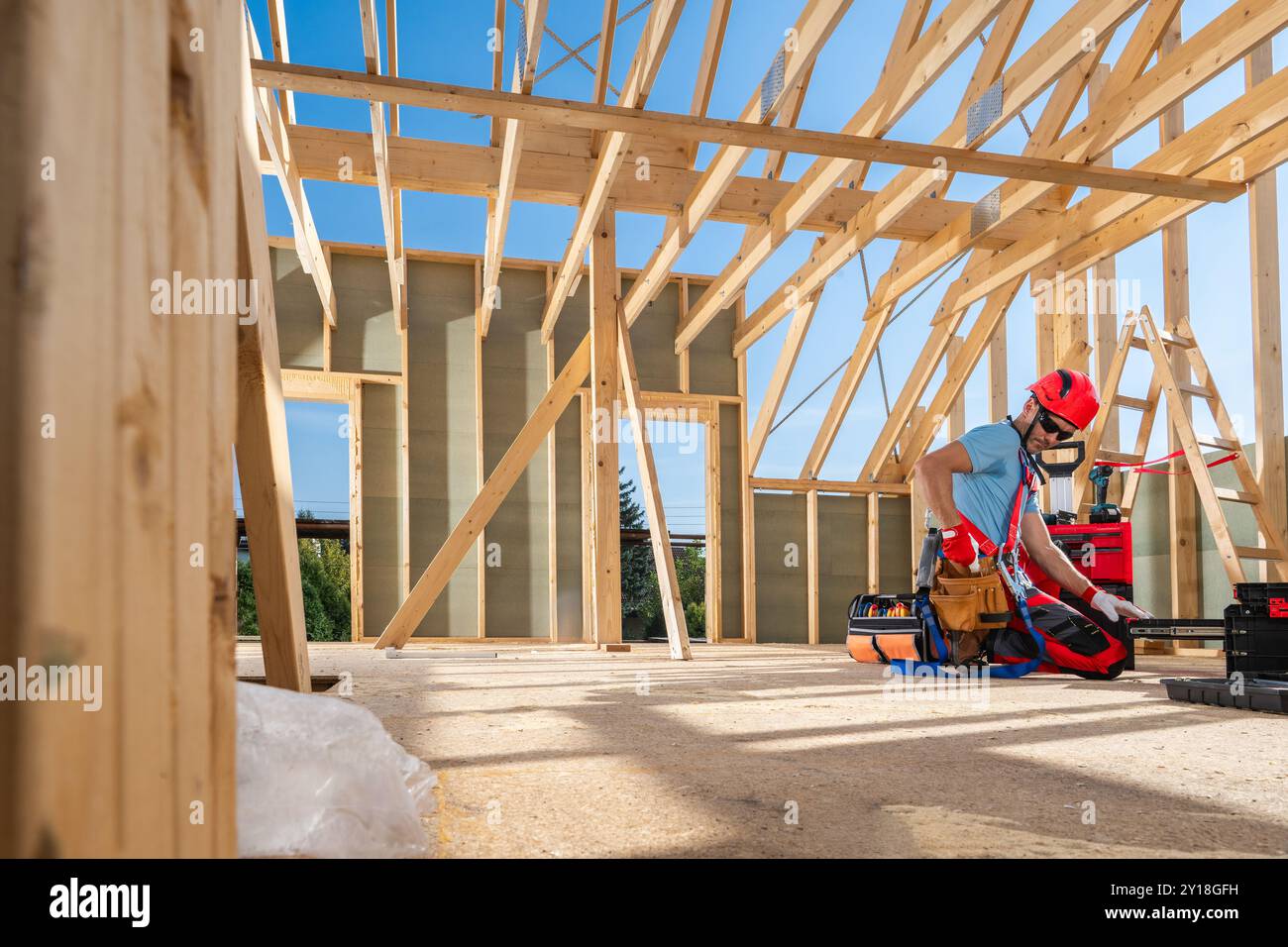 A construction worker in a hard hat is focused on securing wooden beams ...