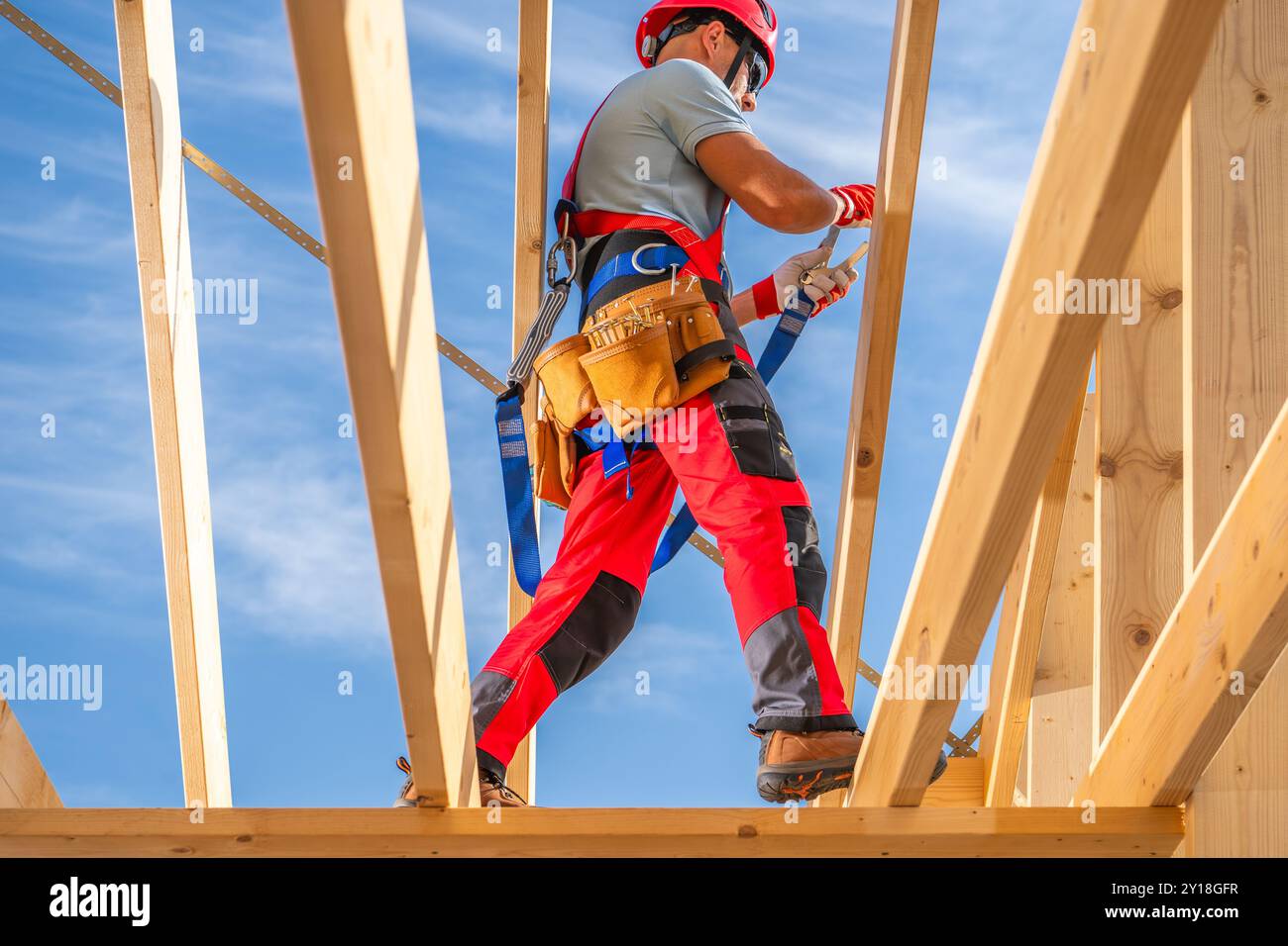 A construction worker is carefully walking on wooden rafters, wearing ...