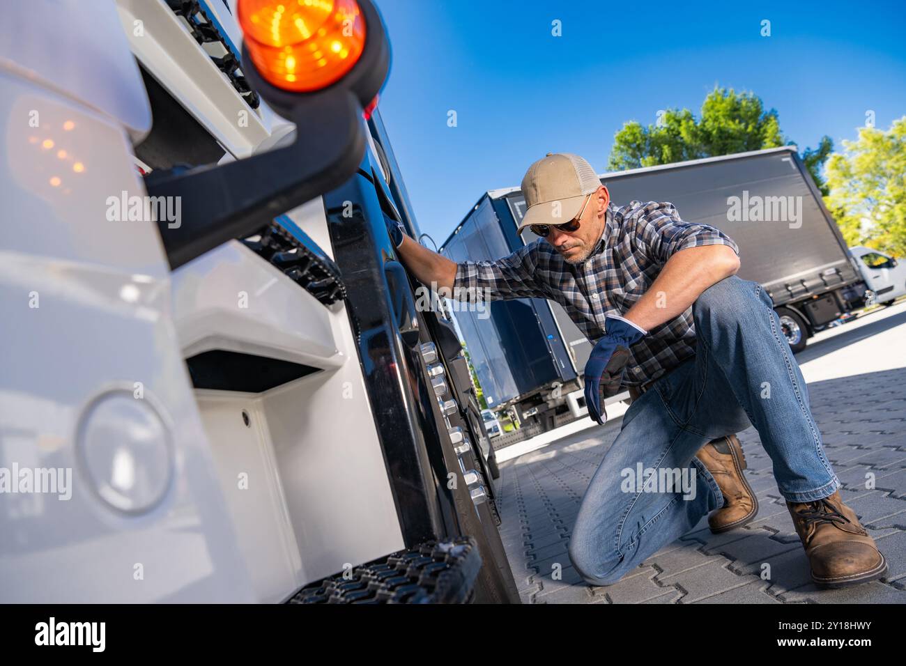 A mechanic kneels beside a truck, inspecting its rear lights in a busy ...