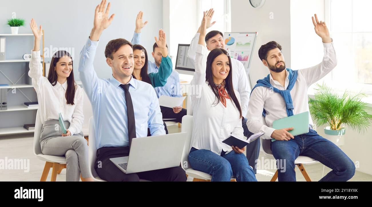 A group of employees are sitting on chairs in an auditorium and raising ...