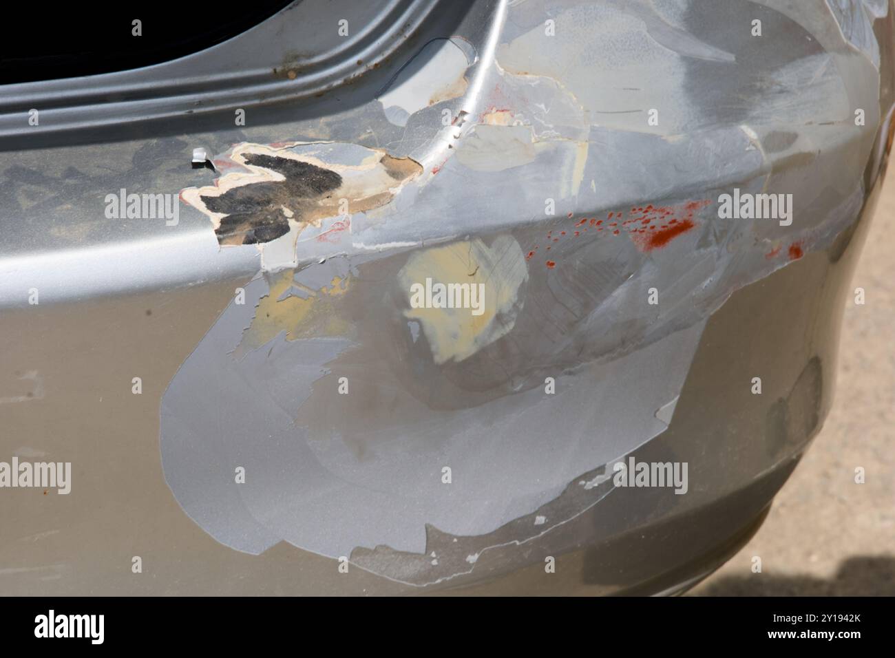 A silver car bumper shows signs of damage with scratches, peeling paint ...