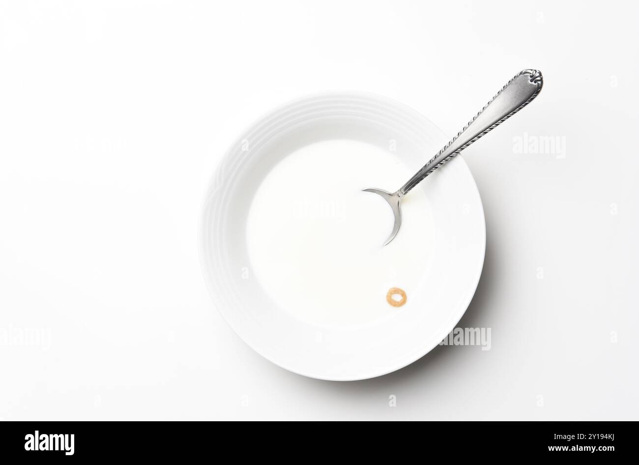 Flat lay white cereal bowl with spoon and one piece of cereal floating ...