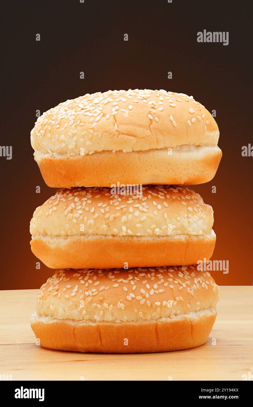 A stack of three hamburger buns with sesame seeds on a rustic wood ...