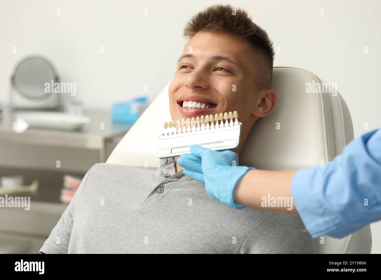Doctor checking young man's teeth color in clinic, closeup. Dental ...