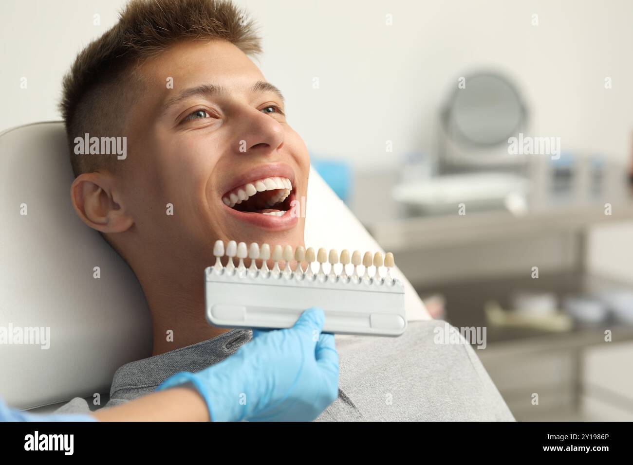 Doctor checking young man's teeth color in clinic, closeup. Dental ...
