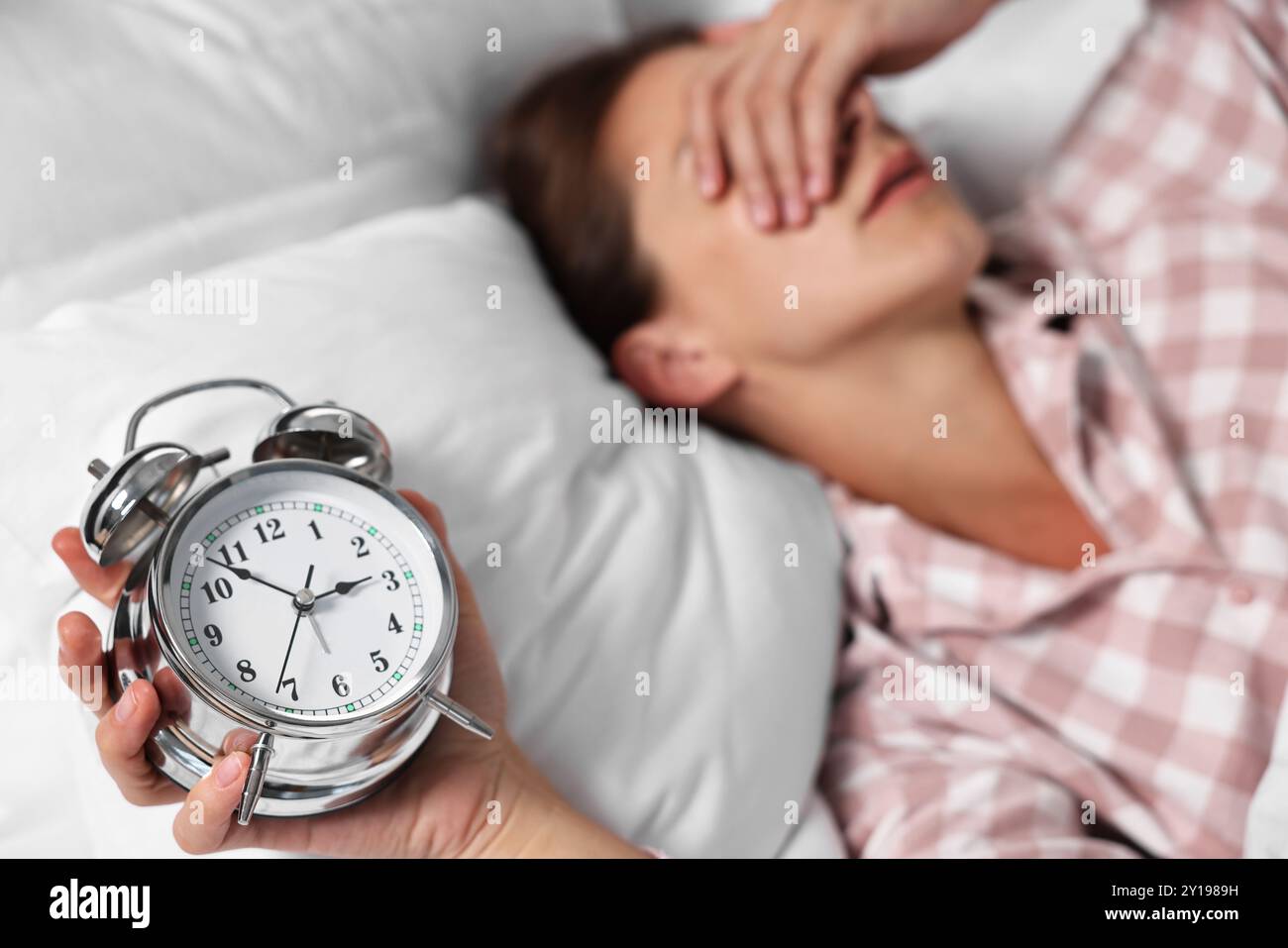 Woman waking up with alarm clock in bed at lunch time, selective focus ...