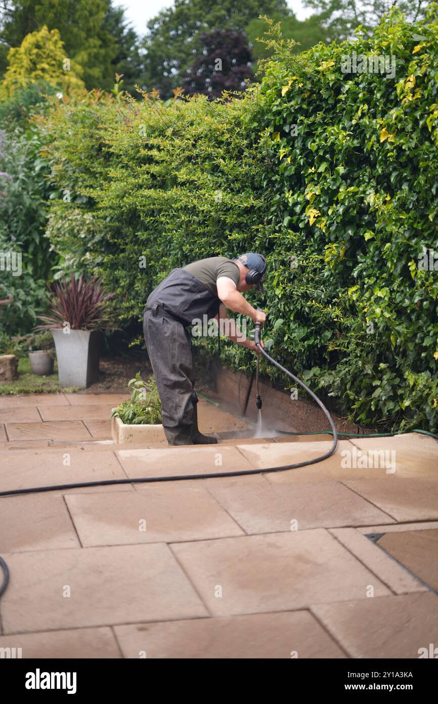 A man cleaning a patio in a garden or backyard with a pressure washer ...