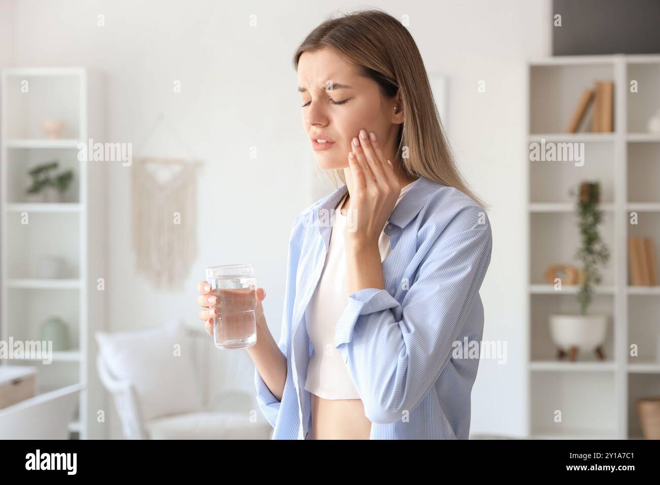 Young woman with glass of cold water suffering from tooth ache at home ...