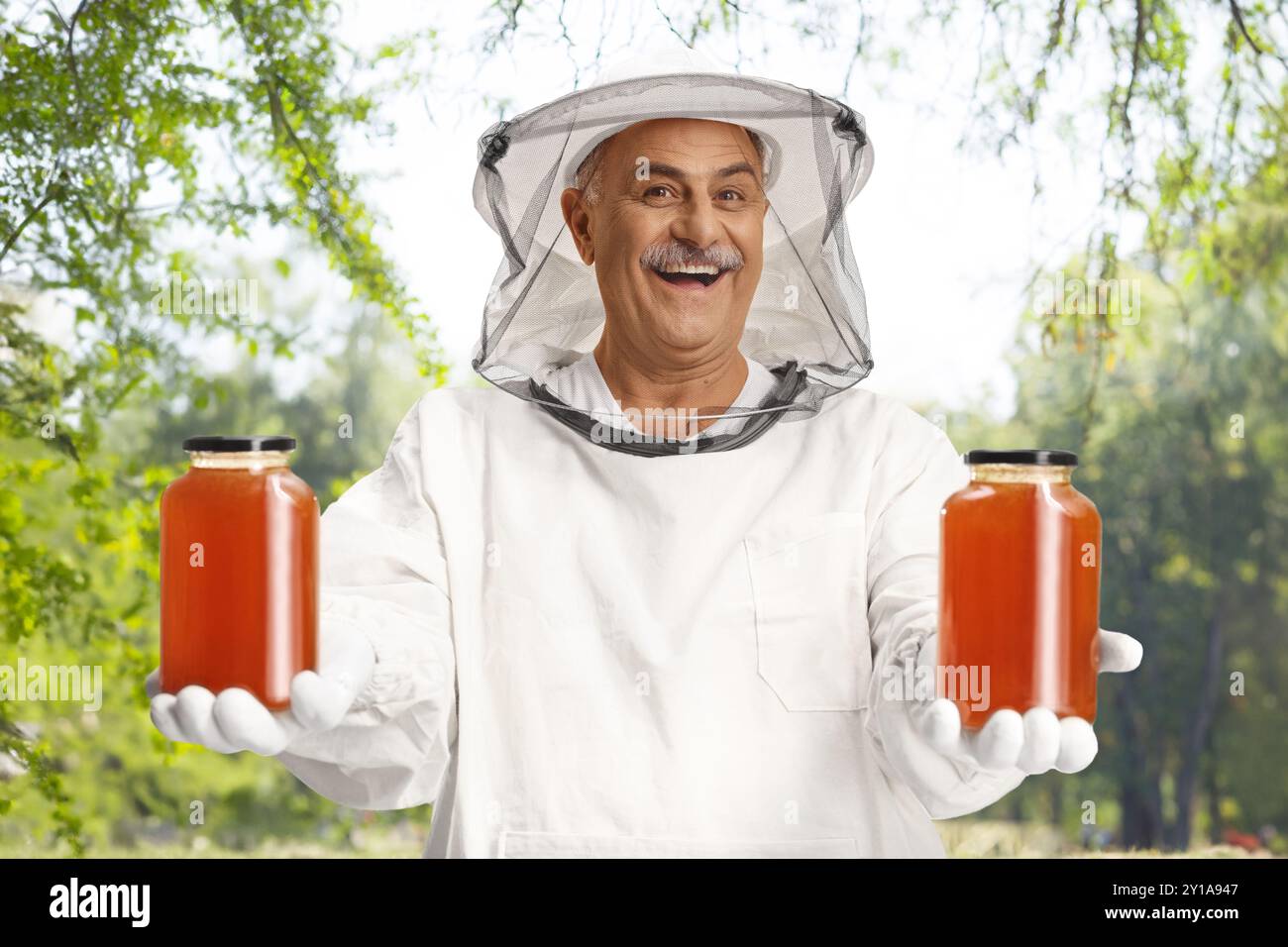 Happy male bee keeper in a uniform holding honey jars and smiling Stock ...