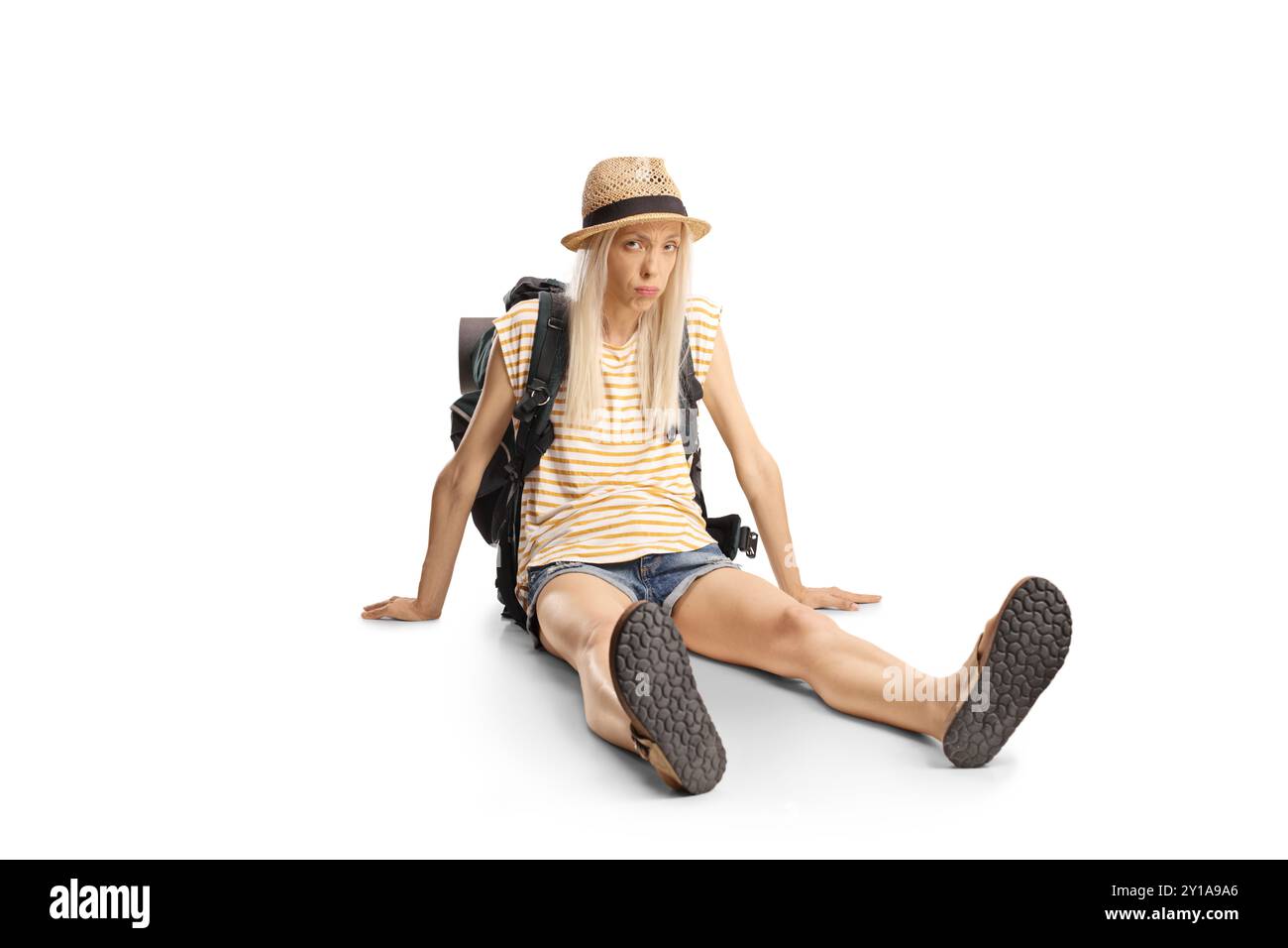 Tired grumpy female tourist with a backpack sitting on the ground ...