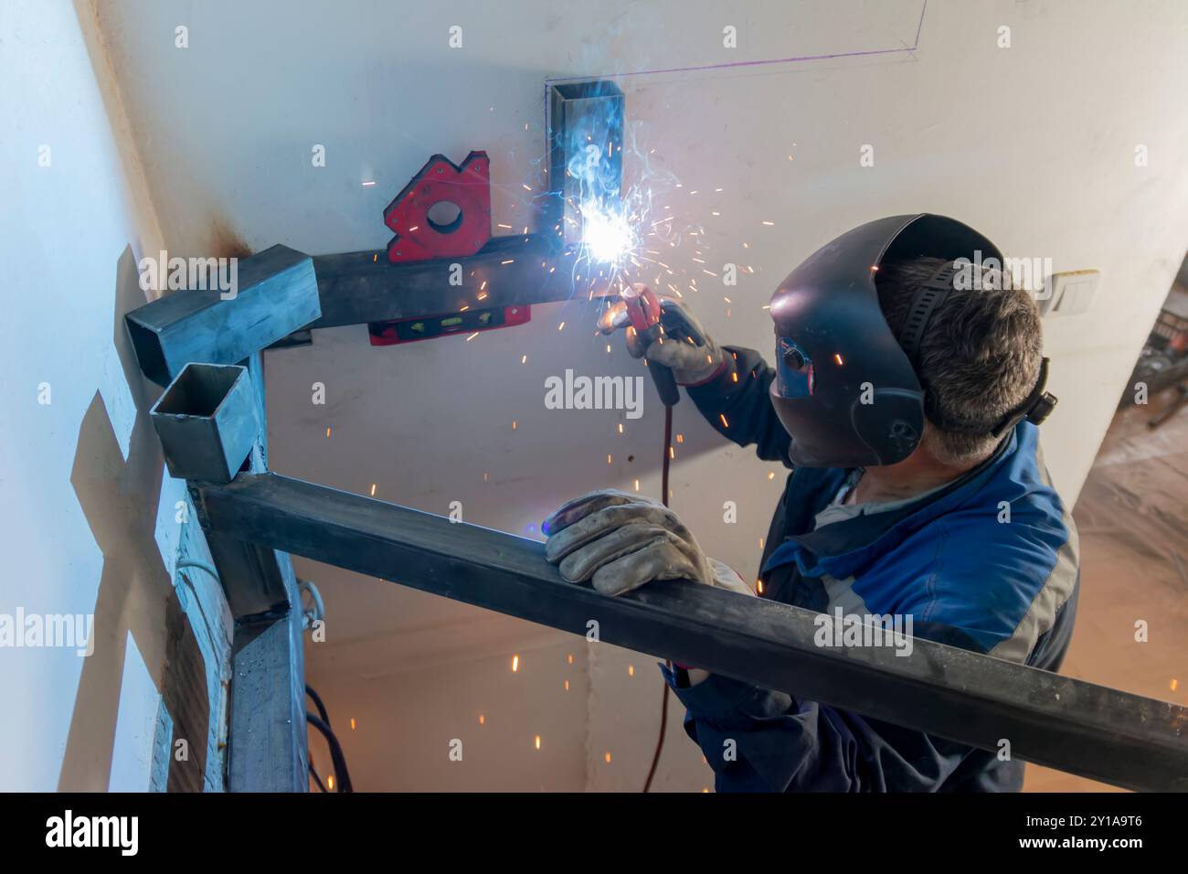 A mature man welder in blue uniform, welding metal with a arc welding ...