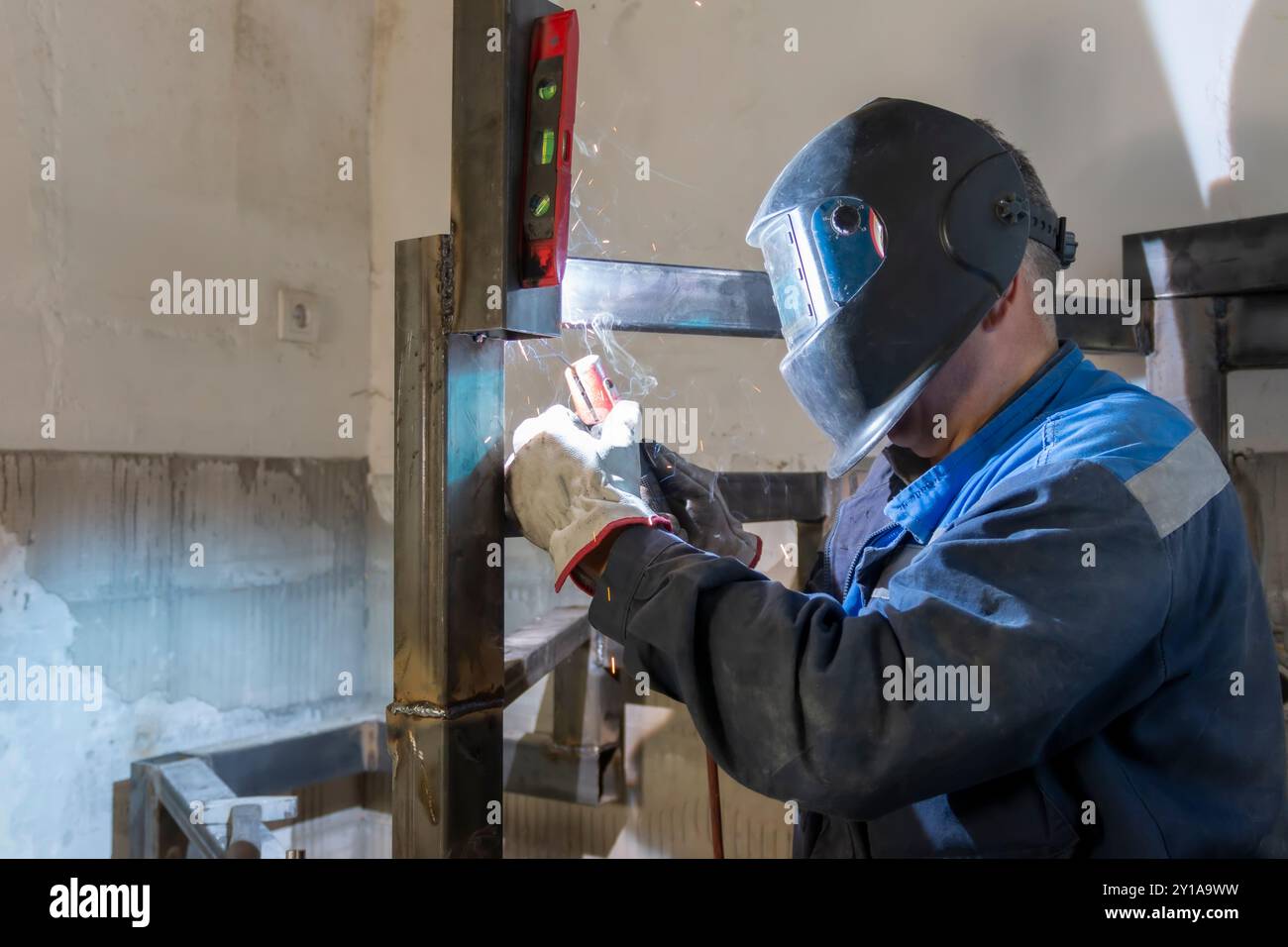 A mature man welder in blue uniform, welding metal with a arc welding ...