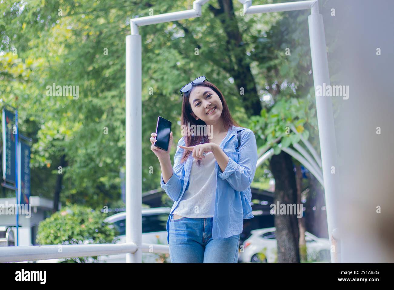 Beautiful Asian woman smiling using glasses pointing at smartphone ...