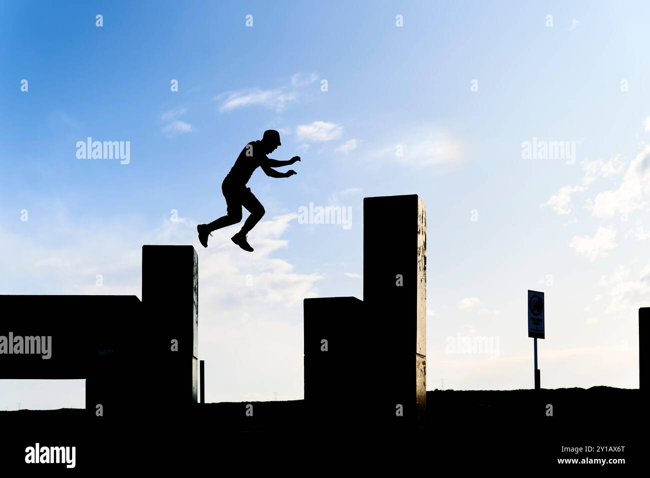 Backlight silhouette of an active man jumping between concrete blocks ...