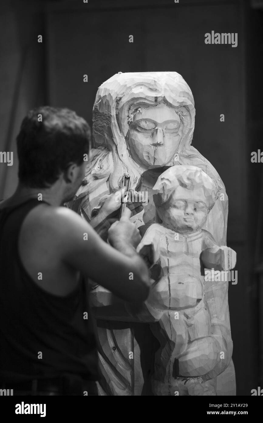 A craftsman carefully carves a wooden statue with a mallet and chisel ...