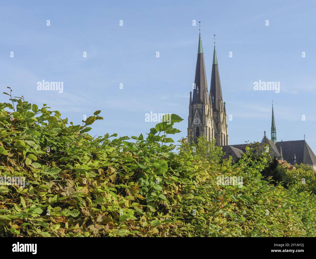 Church towers rise above a green hedge under a clear blue sky ...