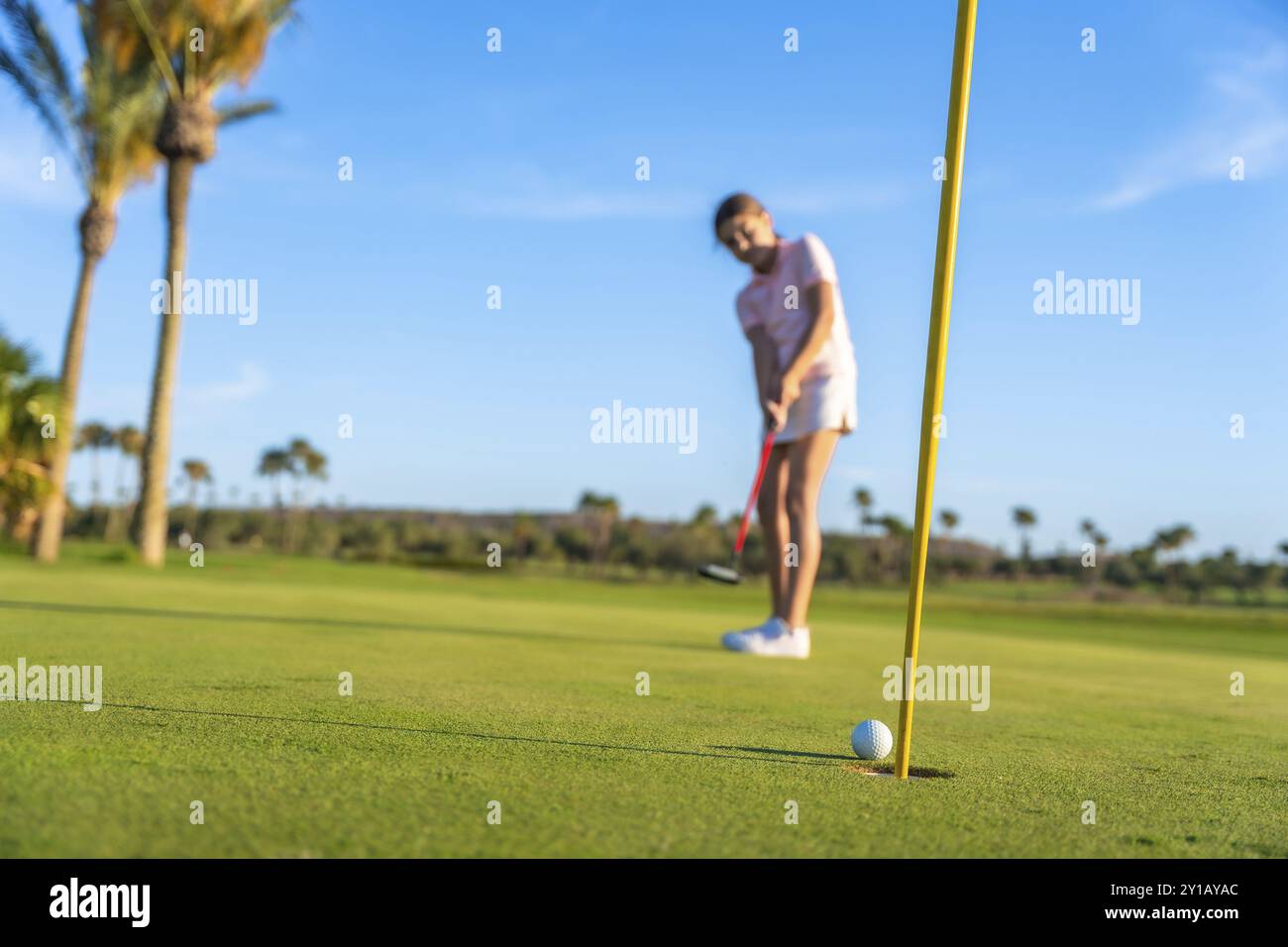 Horizontal photo with focus on the hole while young female golfer ...