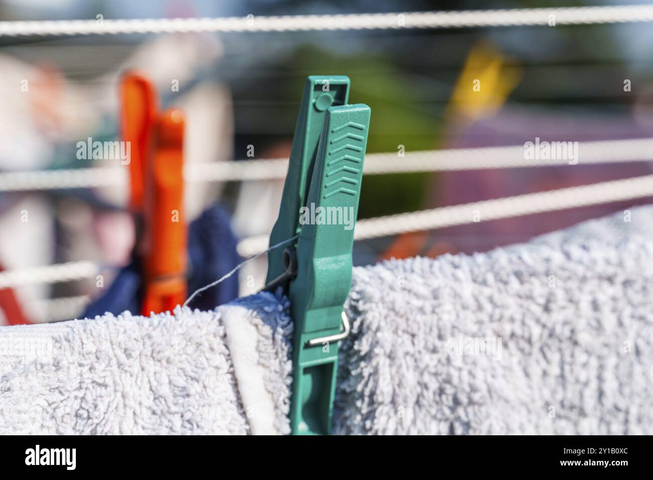 Green clothes peg fixing a towel on a washing line, colourful blurred ...