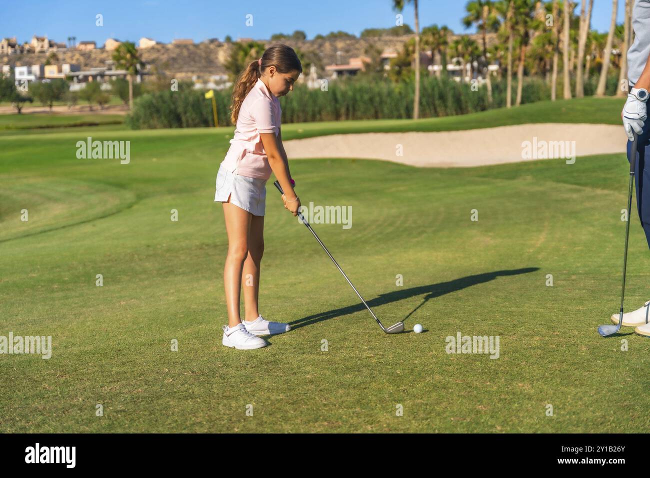 Full length photo of a blonde girl swinging golf next to instructor in ...