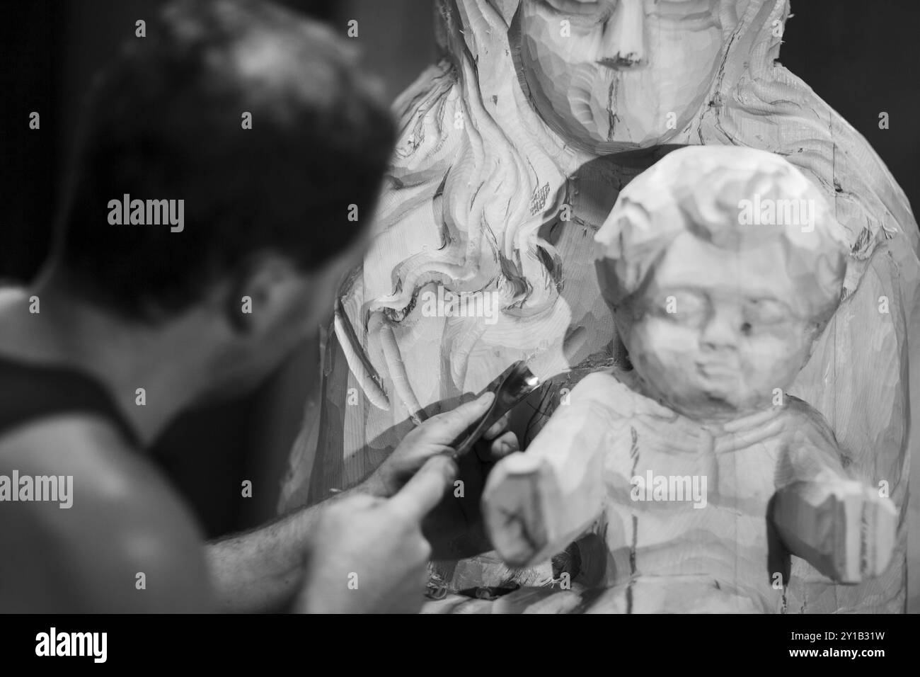 An artist focusing on carving details into a wooden sculpture, captured ...