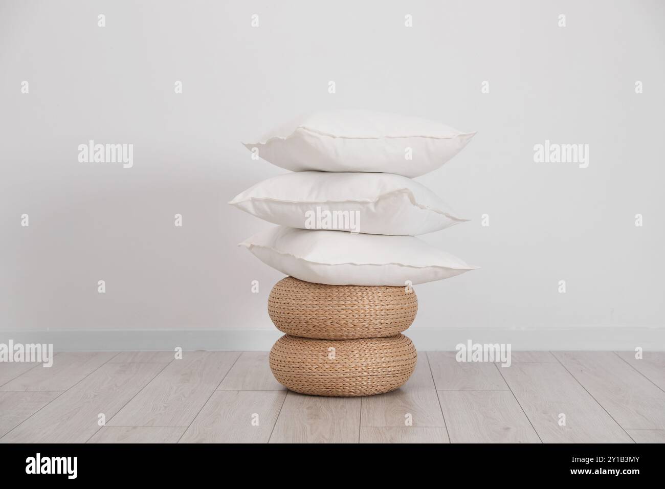 Stack of clean pillows on wicker poufs near white wall Stock Photo - Alamy